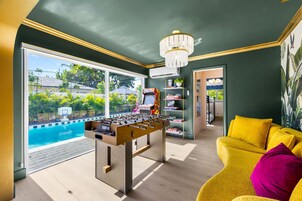 Uma sala de estar moderna com mesa de futebol, um sofá amarelo e vista para uma piscina.