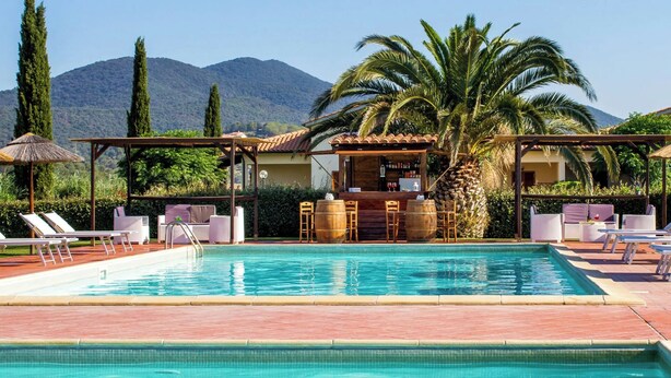 Uma área de piscina com espreguiçadeiras, um bar e montanhas ao fundo.