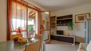 Uma área de refeições com uma mesa posta para dois, um sofá e uma TV sobre um armário.