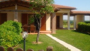 Uma casa de dois andares com um pátio, uma árvore pequena e um gramado bem cuidado.