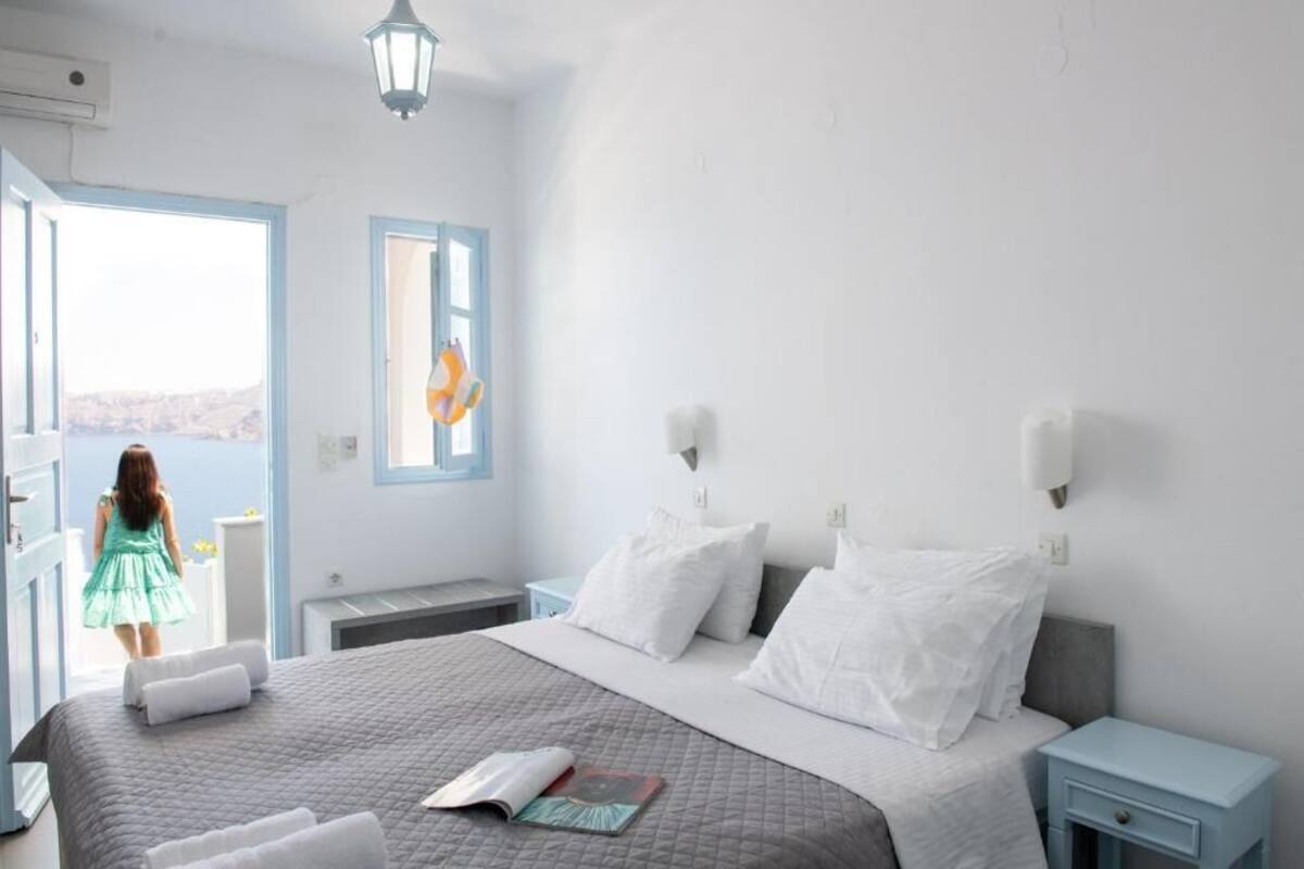 Quarto com cama, duas mesinhas de cabeceira, um criado-mudo, janela com vista e porta.