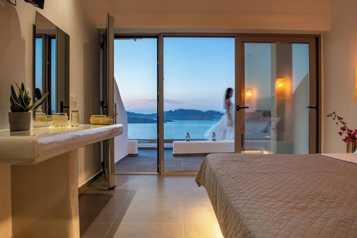 Quarto com cama grande, banheiro com banheira e porta de vidro deslizante para uma varanda com vista para a água.