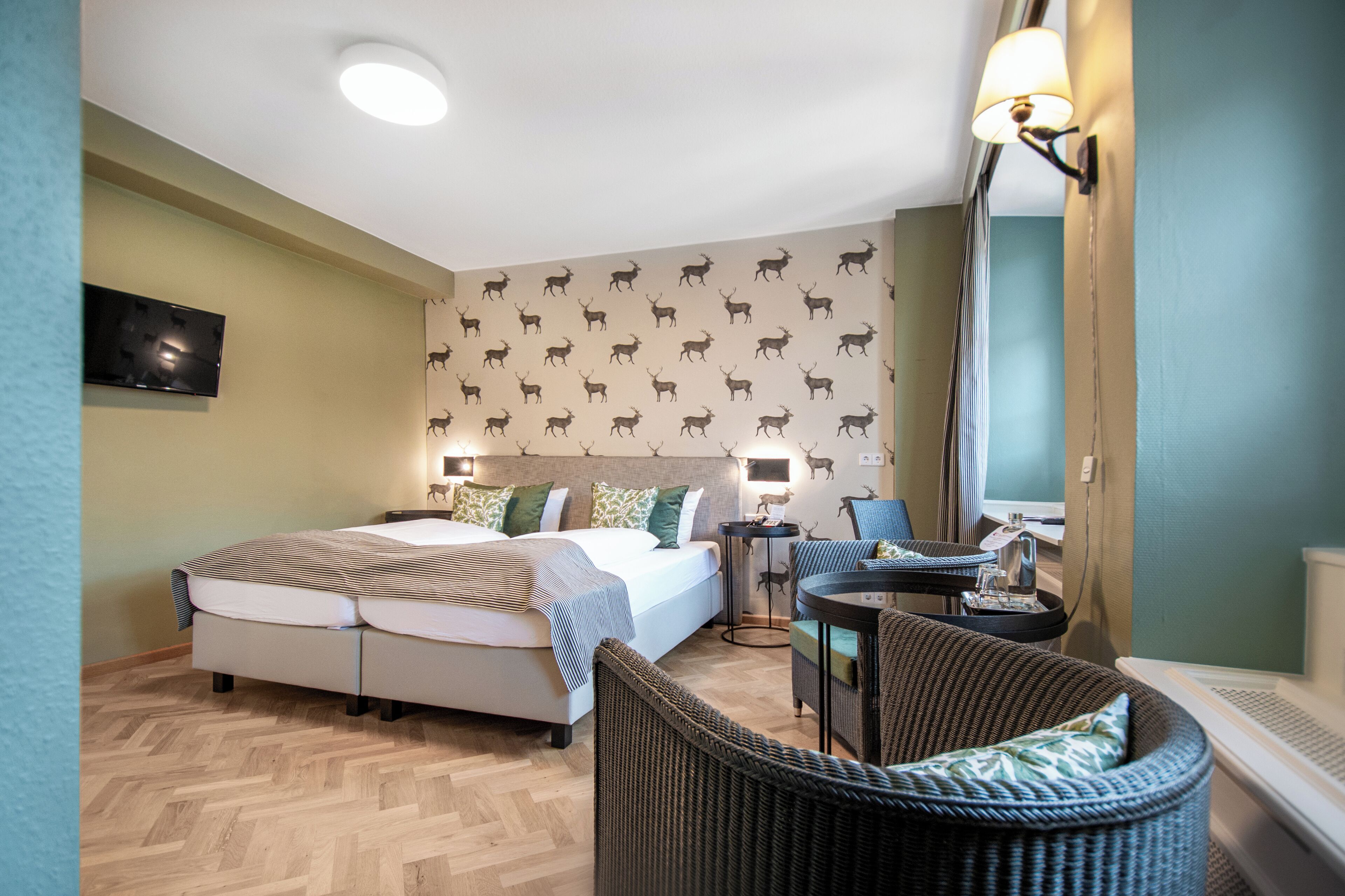 Quarto de hotel com cama, poltrona, mesa pequena e televisão na parede.