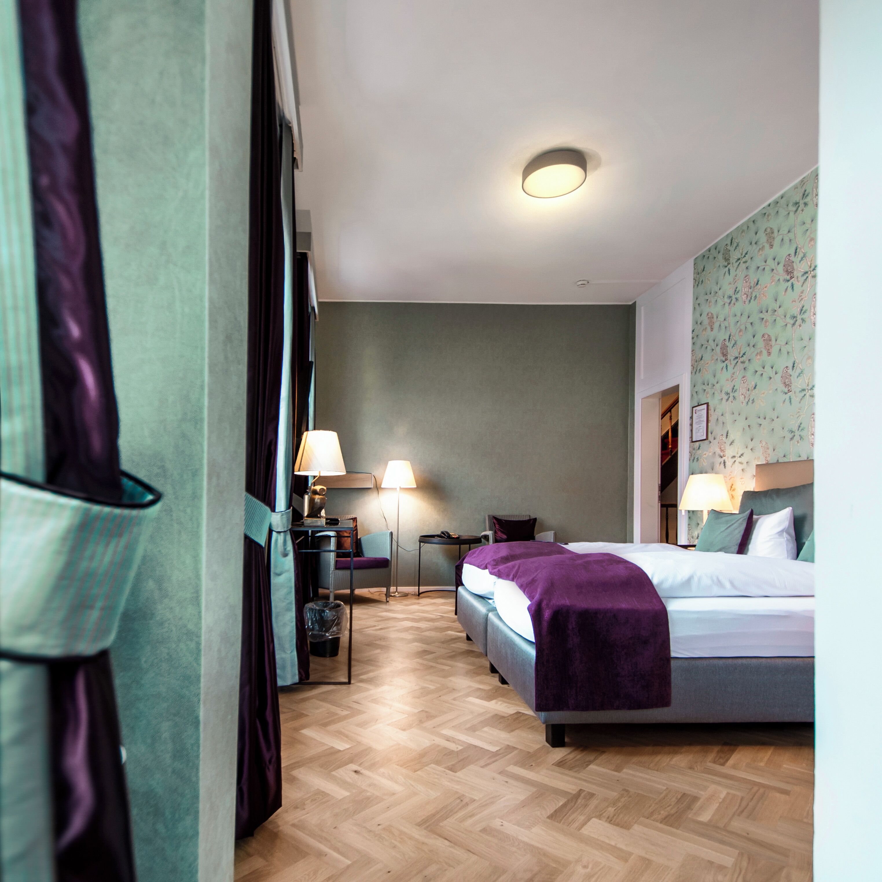 Quarto de hotel com uma cama, uma escrivaninha, uma cadeira, um abajur e uma lixeira.