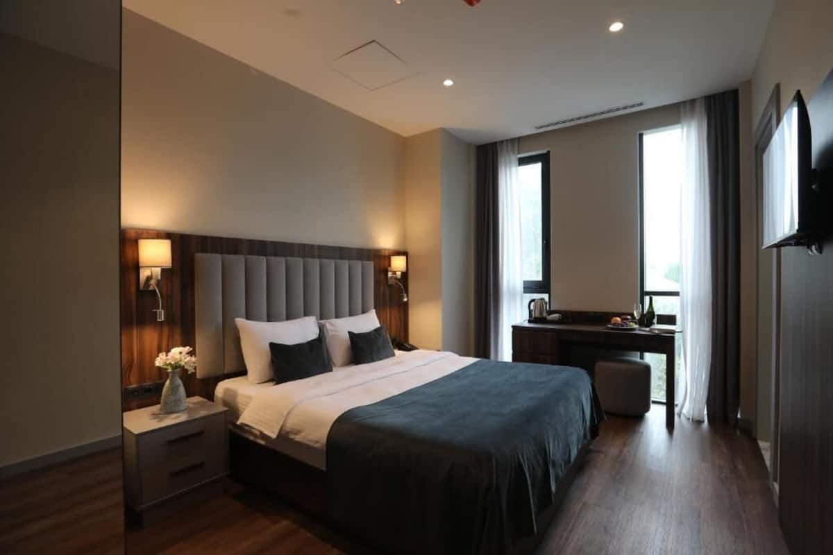 Quarto de hotel moderno com uma cama grande, abajures, uma escrivaninha e uma televisão.