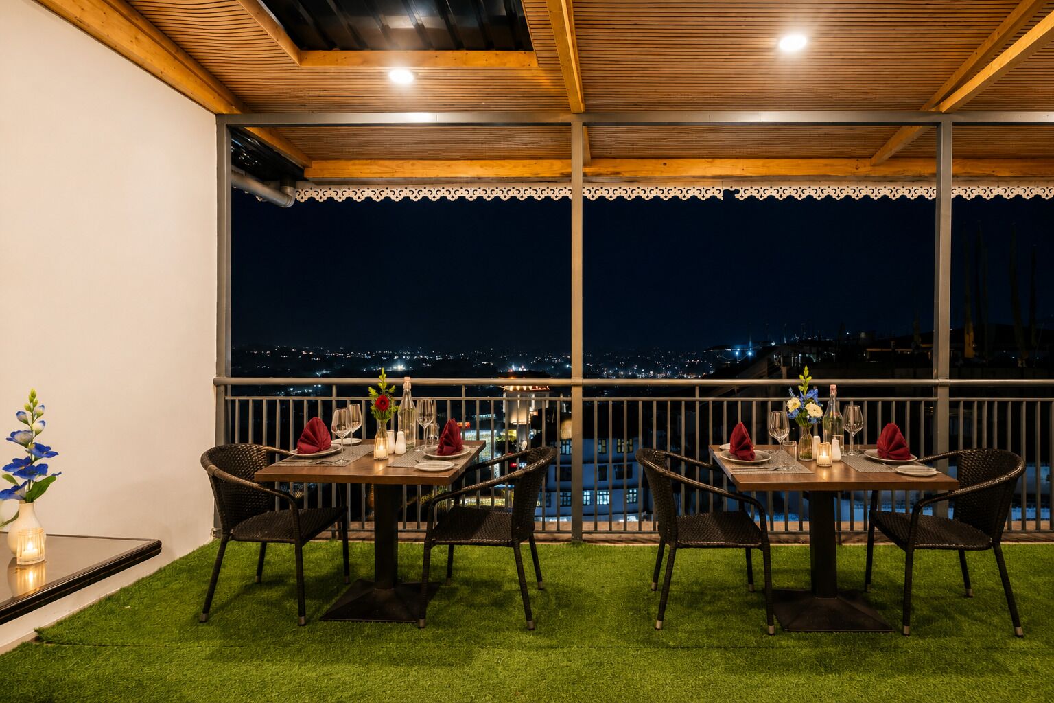 Um restaurante com duas mesas preparadas para refeições, com vista para o horizonte urbano à noite.