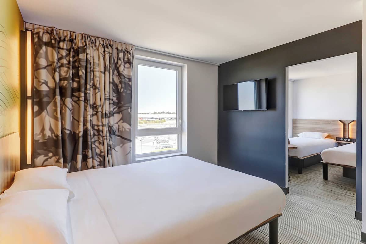 Quarto de hotel com uma cama grande, televisão na parede e vista para a cidade pela janela.