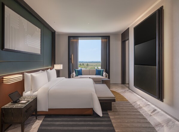 Quarto de hotel com cama grande, sofá, televisão e vista para o exterior.