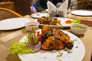 Uma mesa de jantar com pratos de comida, incluindo frango grelhado e legumes, e acompanhamentos.