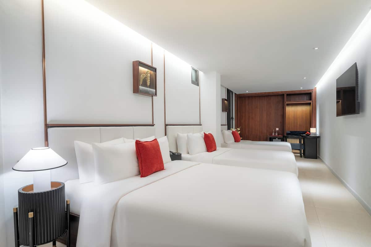 Quarto de hotel com três camas, uma escrivaninha e televisão.
