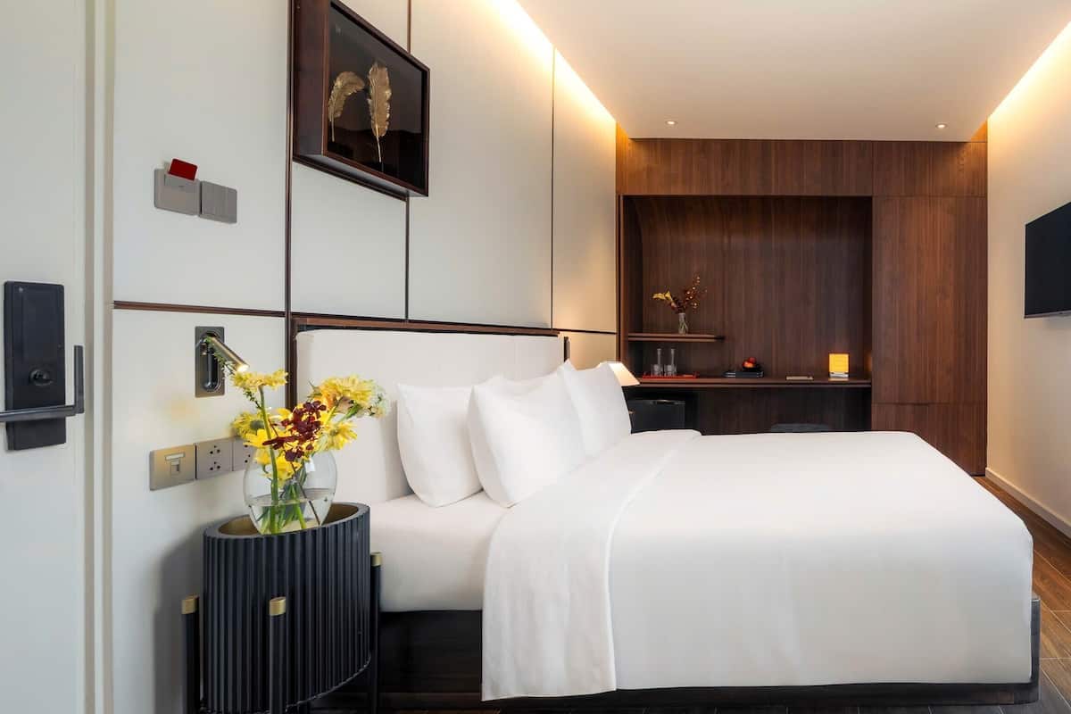 Quarto de hotel moderno com uma cama grande, mesa de cabeceira e uma pequena área de trabalho.