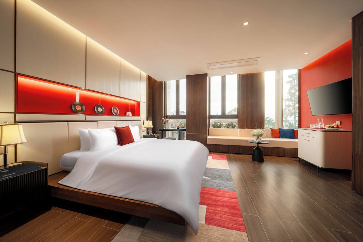 Quarto de hotel moderno com cama grande, televisão, área de refeições e vista para o exterior.