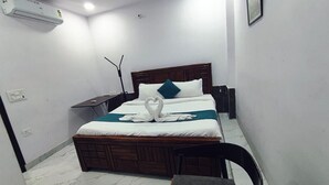 Quarto de hotel com cama de madeira, roupa de cama branca, manta verde-água, arranjo de toalhas em formato de coração, escrivaninha e uma cadeira.