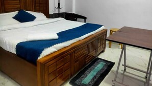 Quarto com cama de madeira, uma mesinha, um porta-roupas e um tapete preto e branco.