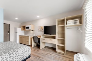 Quarto compacto com cama, cozinha compacta, escrivaninha, TV e estantes embutidas.