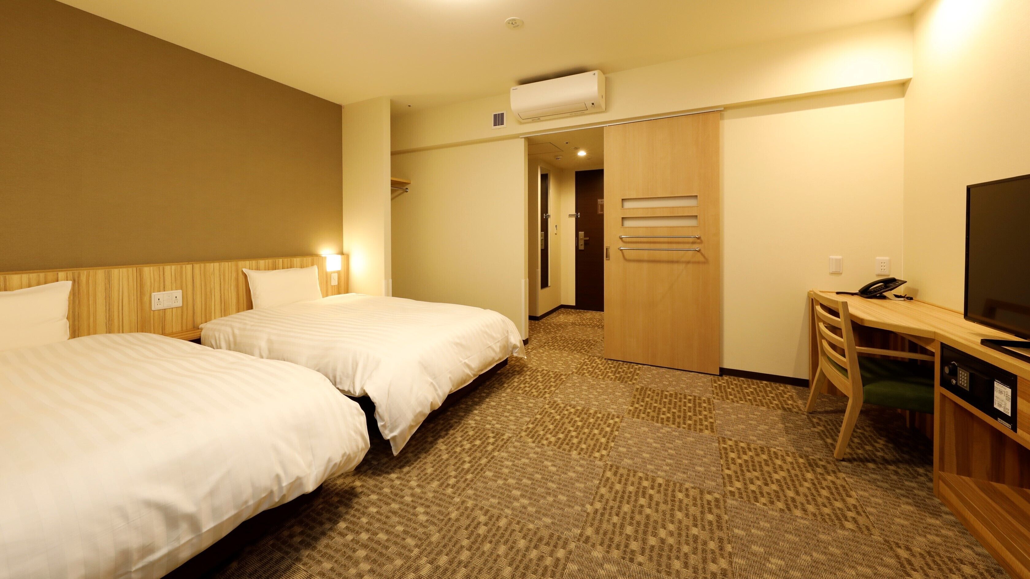 Quarto de hotel com duas camas, uma escrivaninha, uma televisão e um aparelho de ar condicionado.