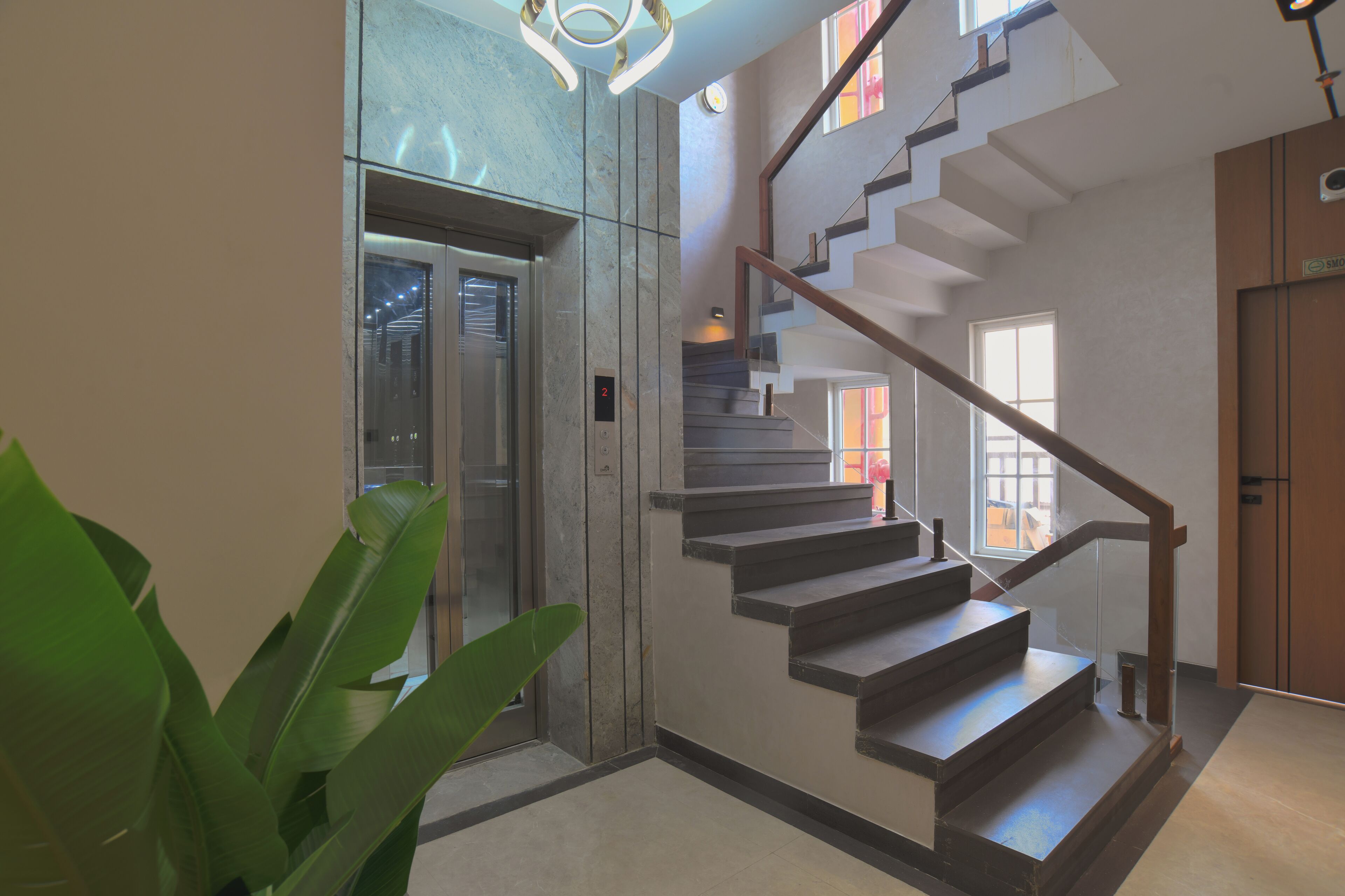 Interior moderno com escada, elevador e uma grande planta em vaso.