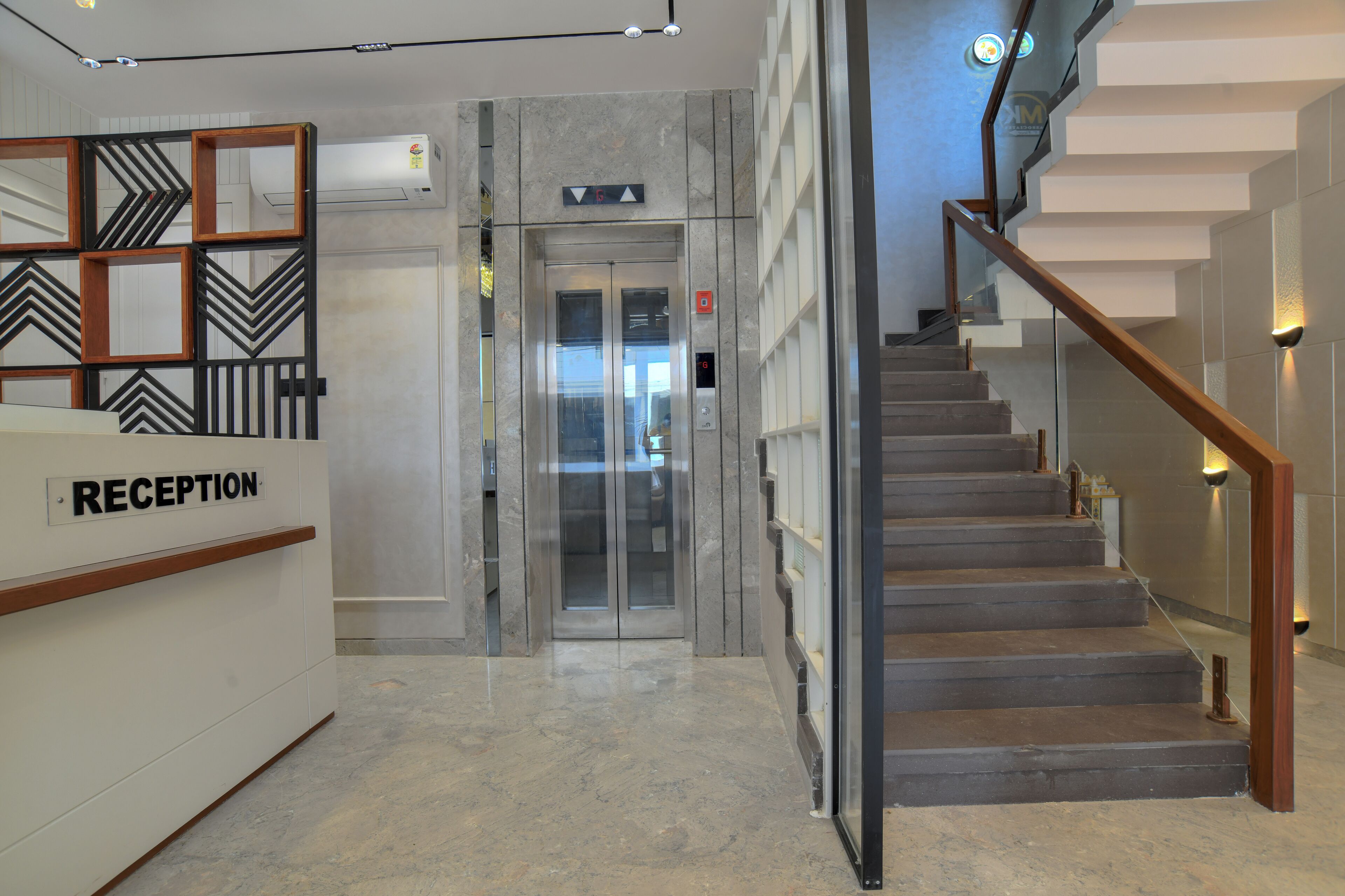 Uma área de recepção com balcão de atendimento identificado como "RECEPTION", uma escada com corrimãos de madeira e um elevador com parede espelhada.
