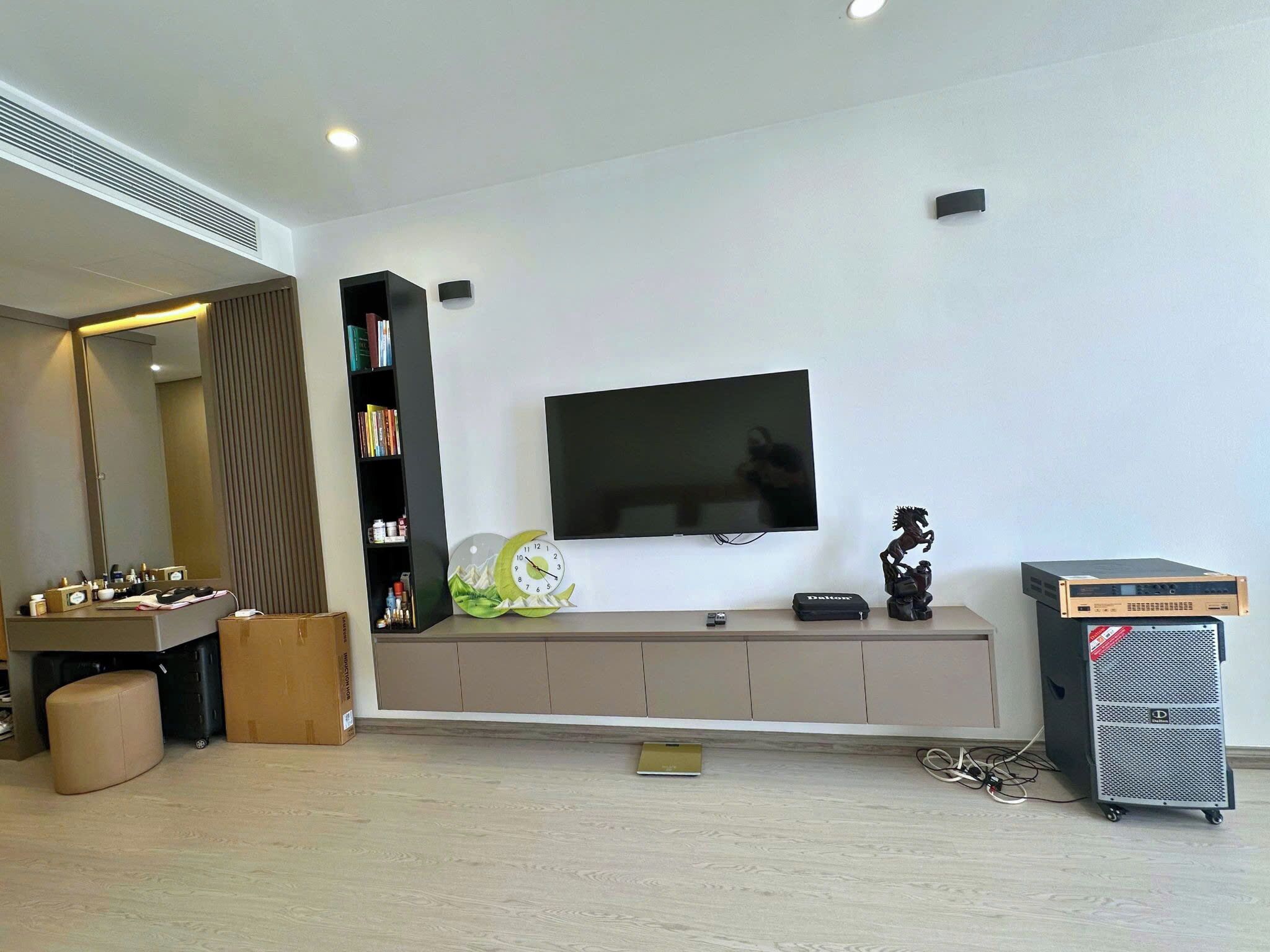 Uma sala de estar moderna com televisão de tela plana fixada na parede, uma estante de livros, uma pequena estátua e um sistema de som.