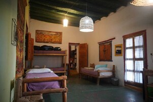 Quarto rústico com beliches, um armário de madeira, luminária pendente e uma pintura grande na parede.