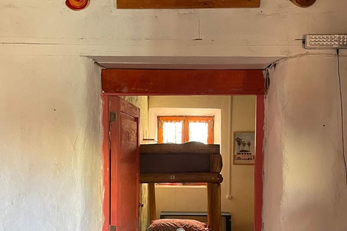 Quarto com beliche, placa de madeira acima da porta e janela com cortinas.