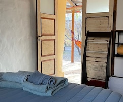 Quarto com cama, porta de madeira e vista para o exterior.