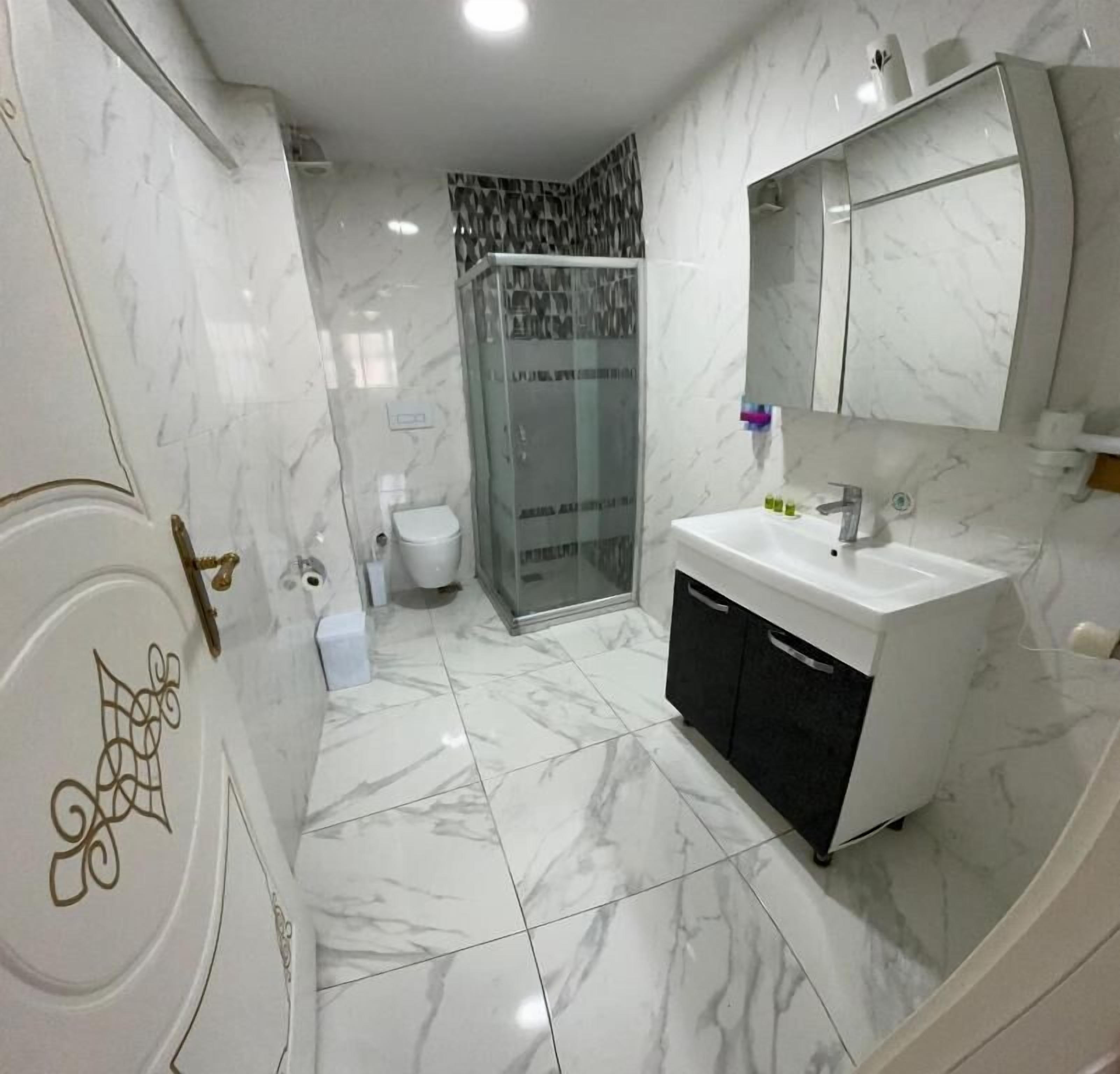 Um banheiro moderno com piso de mármore branco, box de vidro, pia branca com armário preto e um espelho grande acima da pia.