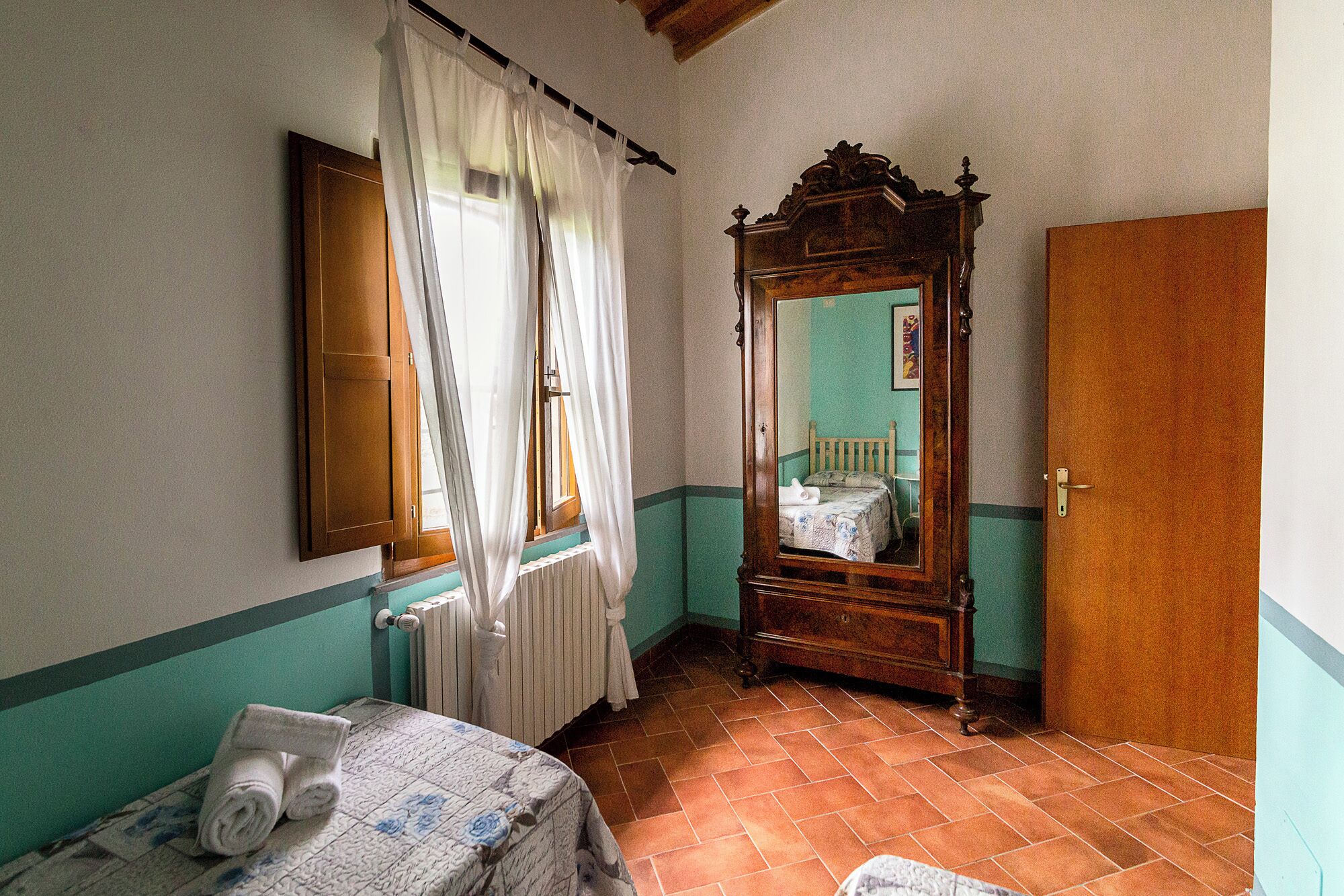 Quarto com cama de madeira, um espelho grande, armário de madeira e janela com cortinas.