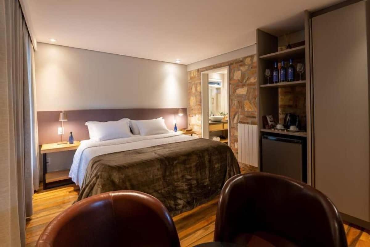 Quarto de hotel com cama, mesas de cabeceira, guarda-roupa e um espaço de estar.
