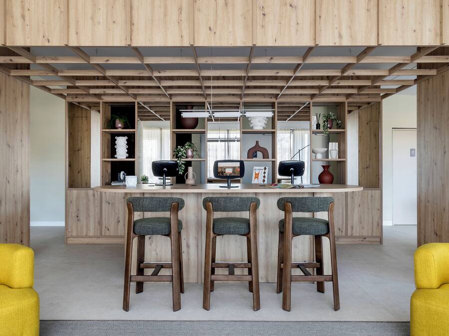 Uma cozinha moderna com armários de madeira, uma ilha central com banquetas e uma estante embutida.