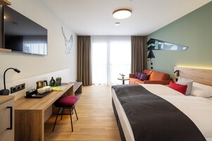 Quarto de hotel com cama, escrivaninha, cadeira, televisão e vista para o exterior.
