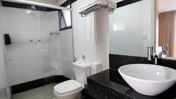 Uma casa de banho moderna com cabine de duche em vidro, sanita branca, lavatório branco e bancada preta.