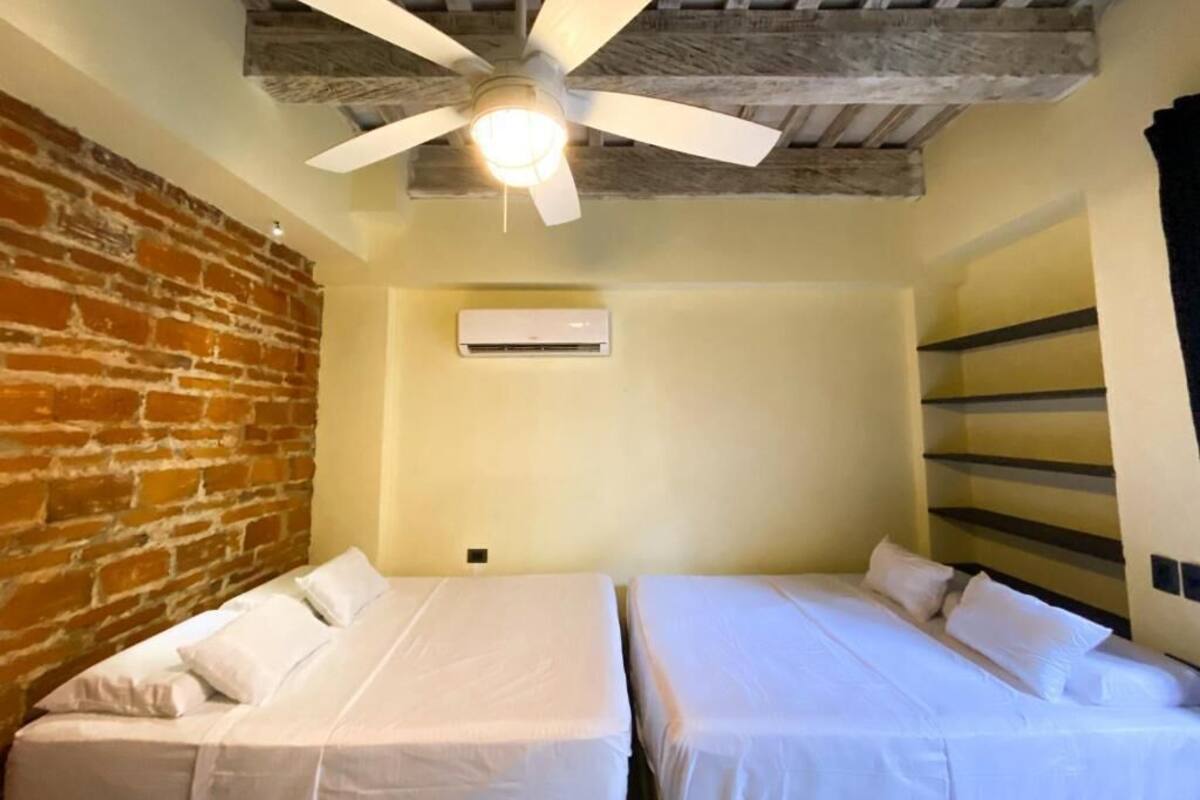Quarto com duas camas, um ventilador de teto e uma parede de tijolos.