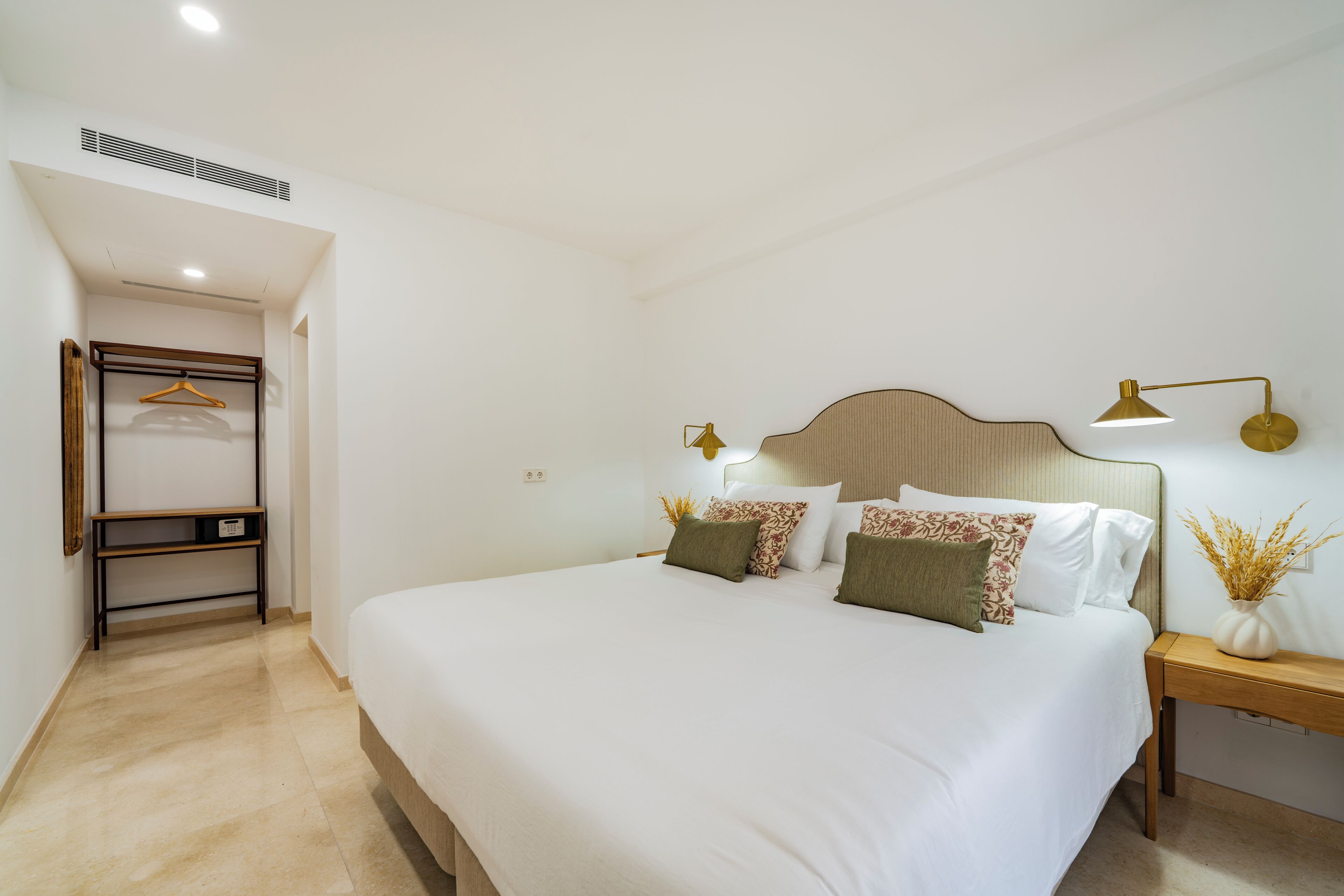Quarto bem arrumado com cama, mesas de cabeceira, guarda-roupa e luminária na parede.