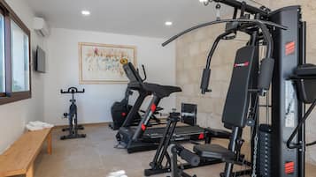 Uma academia com equipamentos de ginástica, um banco e uma TV fixada na parede.