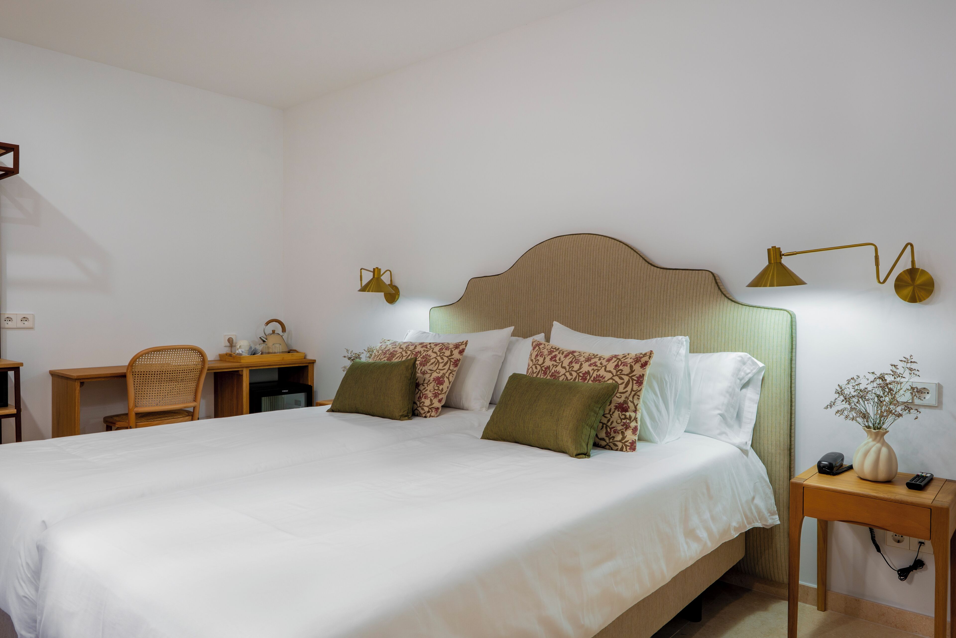 Quarto de hotel bem arrumado, com uma cama grande, mesas de cabeceira, escrivaninha e abajur.