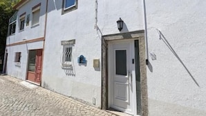 Um edifício de dois andares com fachada branca, rua de paralelepípedos e porta vermelha.