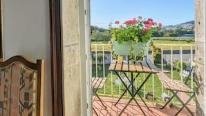 Varanda com vista para uma paisagem verde, uma cadeira de madeira e uma mesa com um vaso de flores.