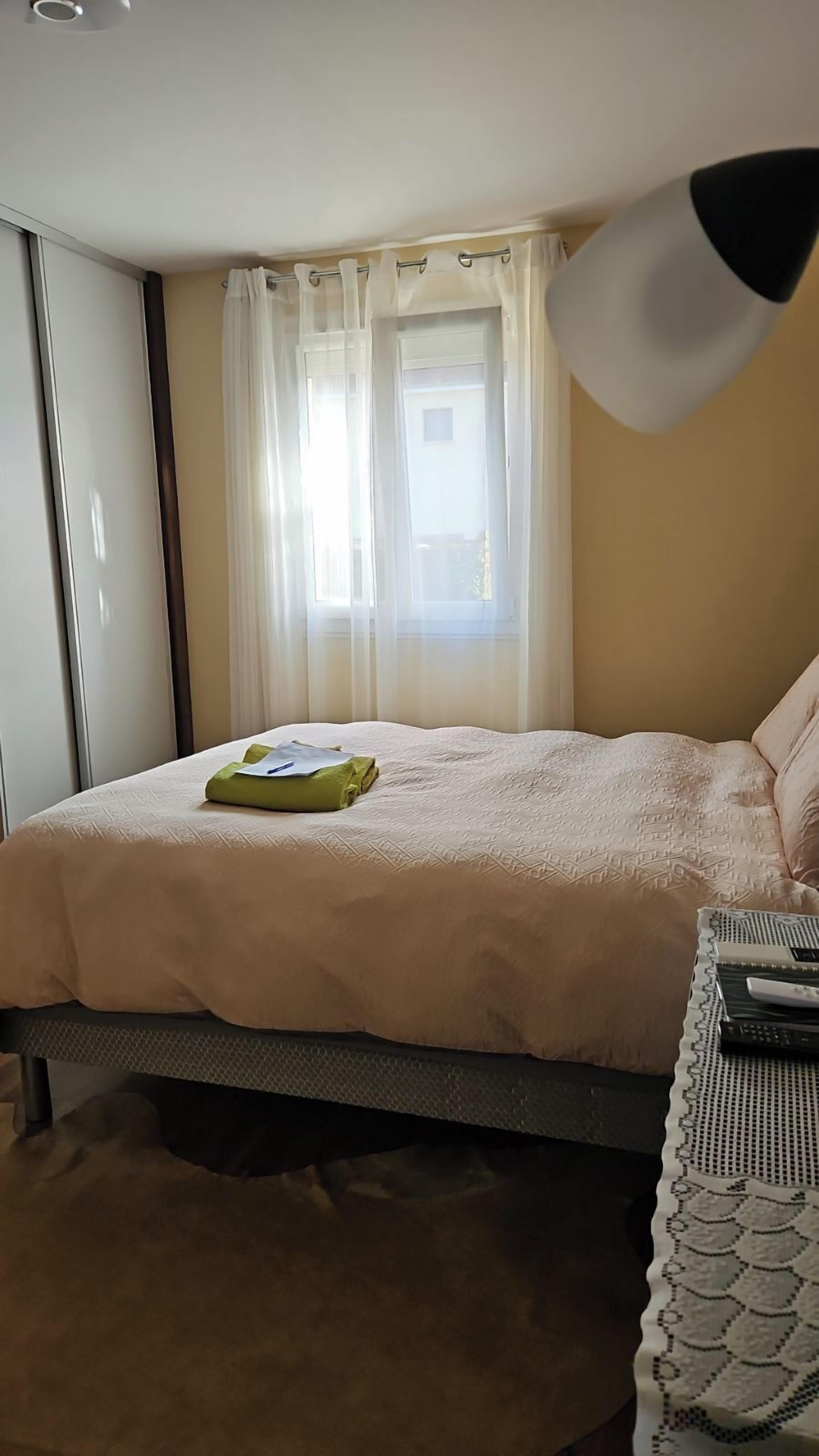 Quarto com cama, mesa de cabeceira com abajur e janela com cortinas.