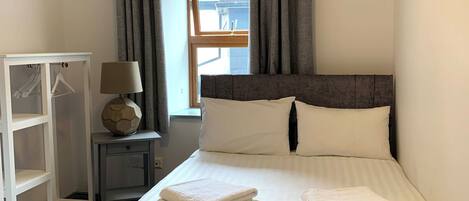 Quarto de hotel bem arrumado, com cama, guarda-roupa, mesa de cabeceira e janela com cortinas.
