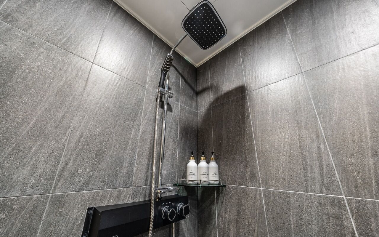 Um chuveiro moderno com chuveiro de chuva, chuveiro manual e borrifador manual. Há três frascos de shampoo e condicionador em uma prateleira.