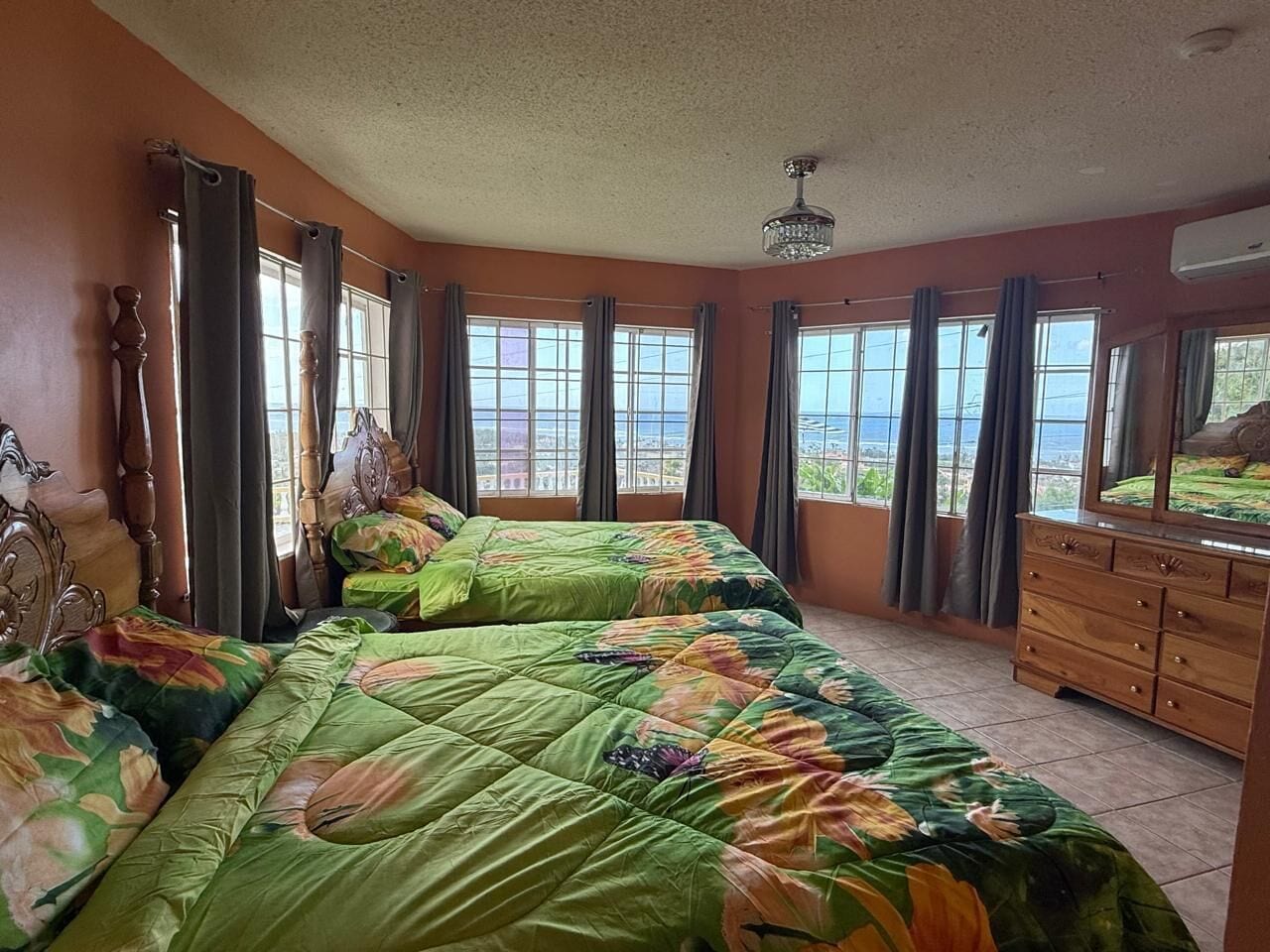 Quarto com duas camas, cômoda e amplas janelas com cortinas.