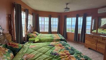 Quarto com duas camas, cômoda e amplas janelas com cortinas.