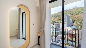 Quarto de hotel moderno com um espelho grande, porta de vidro deslizante para uma varanda e vista dos edifícios e colinas ao redor.