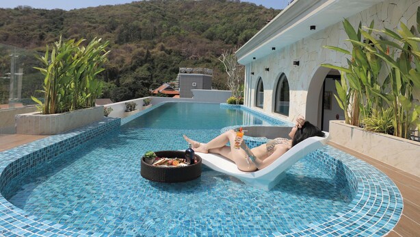 Uma pessoa relaxando em uma cadeira de flutuação na piscina, com uma cesta de petiscos e uma bebida.
