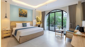 Quarto de hotel moderno com uma cama grande, uma mesa, uma cadeira e vista para o verde através de uma porta de vidro.
