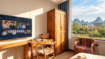 Quarto de hotel com uma secretária de madeira, uma cadeira confortável, uma cama com uma bandeja de chávenas de café, um guarda-roupa e uma janela ampla com vista para a montanha.