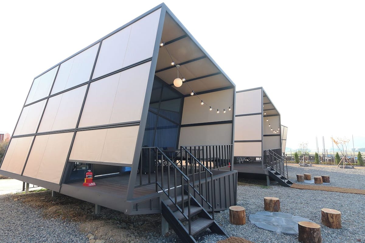 Um edifício moderno com design geométrico, teto plano, janelas amplas e uma escadaria que leva a um terraço.