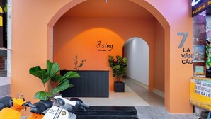 Área de recepção de um hotel boutique com design moderno, apresentando um balcão de atendimento, uma escadaria e uma placa com o nome do hotel.