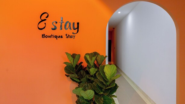 Um corredor com parede laranja e um arco branco. A parede tem uma placa que diz 'Estay Boutique Stay'.